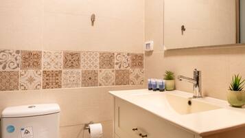 Casa de banho com sanita, lavatório, espelho e azulejos decorativos.