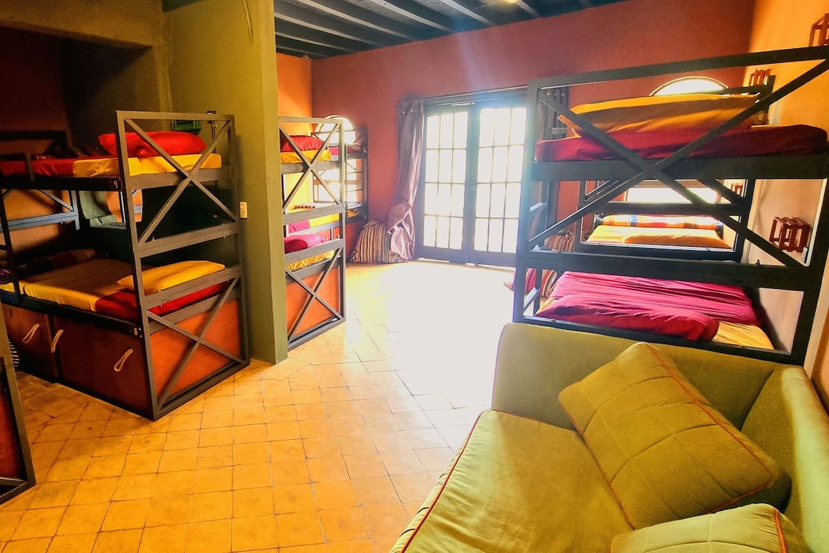 Quarto em dormitório com beliches, um sofá e uma janela com cortinas.