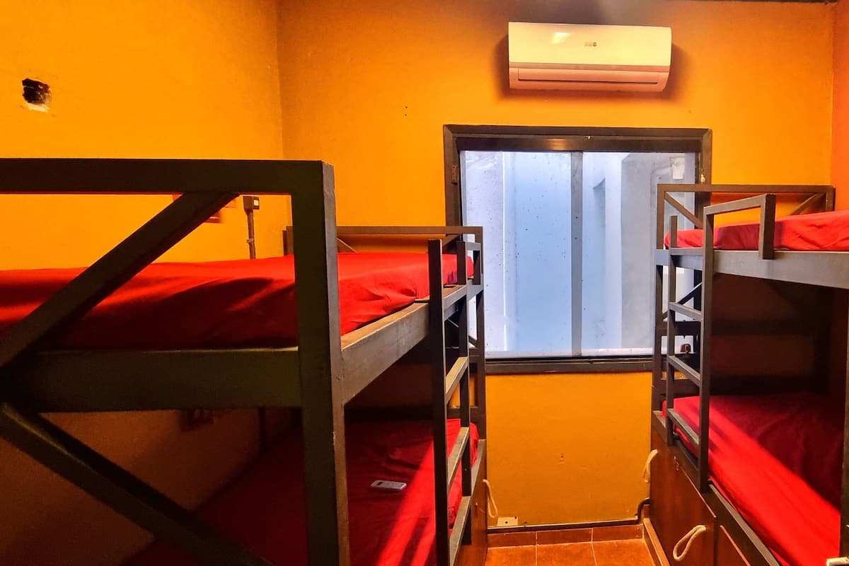 Quarto em dormitório com beliches, ar condicionado e janela.