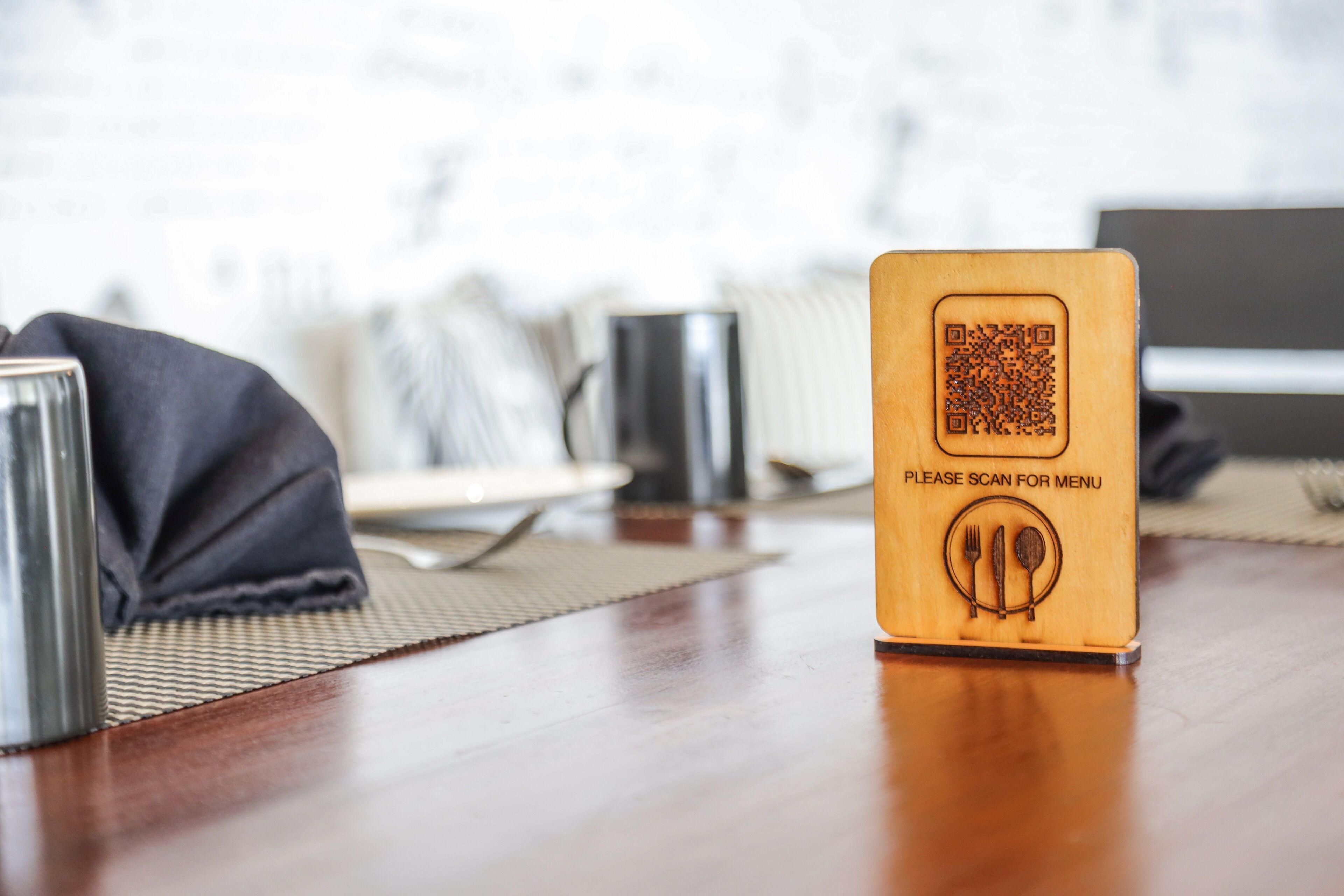 Suporte de menu com código QR de madeira sobre uma mesa de madeira, com fundo desfocado de um quarto.