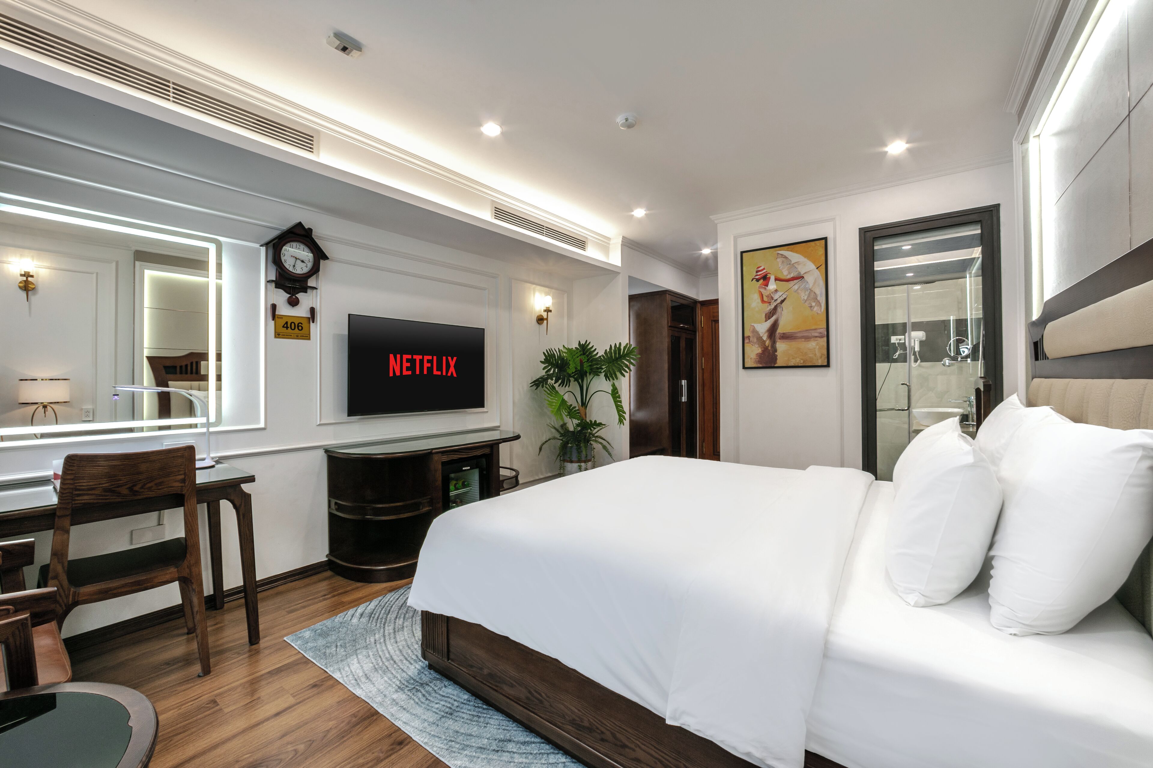 Quarto de hotel moderno com uma cama grande, uma escrivaninha com cadeira, televisão e relógio fixado na parede.