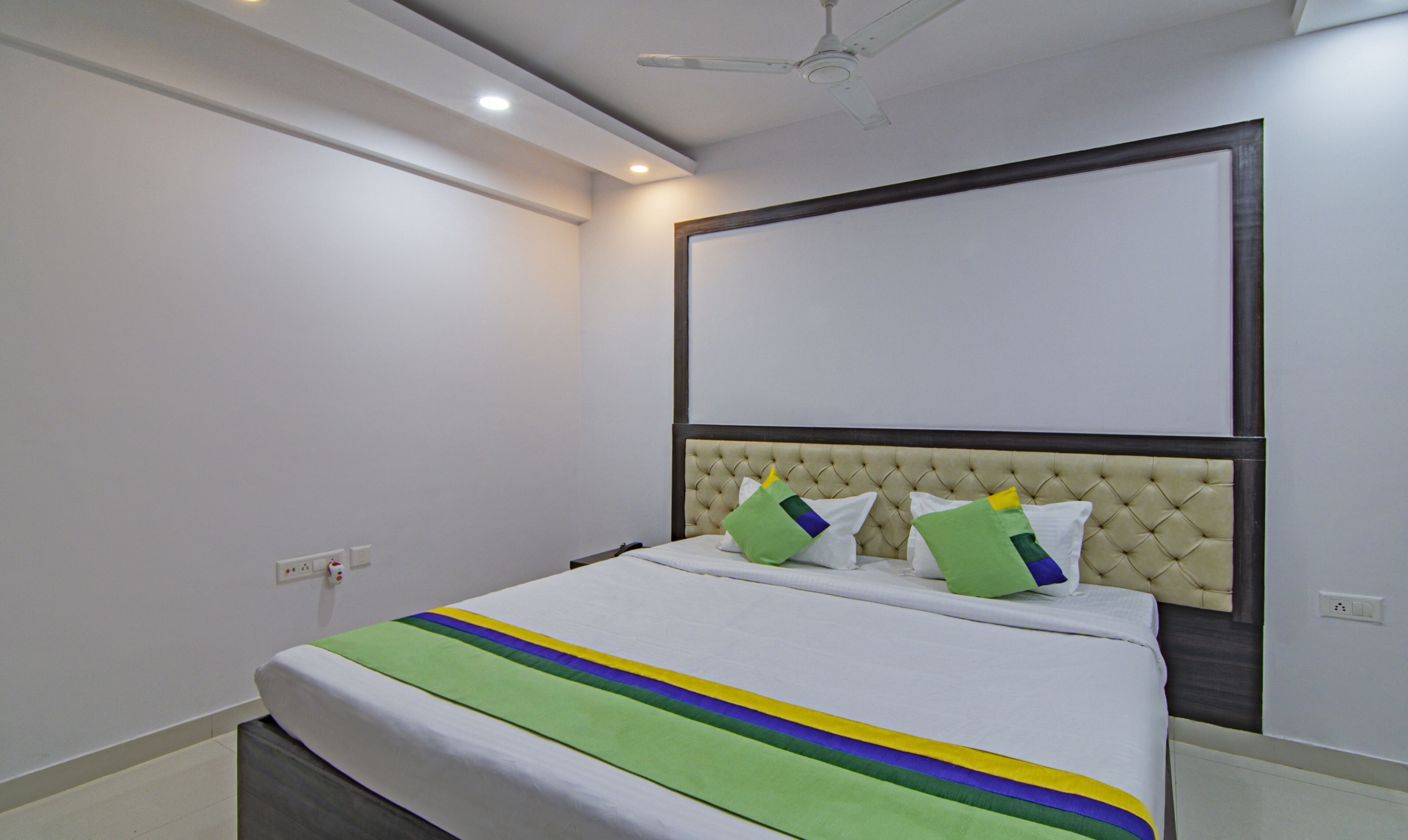 Quarto de hotel com cama, ventoinha no teto e uma janela grande.
