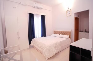 Quarto com cama, guarda-roupa, escrivaninha e kitchenette.