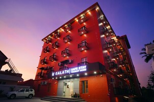 A multi-story building with balconies, a sign reading "KAILATH Safe Stay Tourist Home," and a white car parked in front.