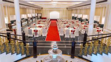 Uma luxuosa sala de baile de hotel, com tapete vermelho, cadeiras brancas e palco central.