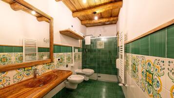 Uma casa de banho com toucador de madeira, uma sanita branca, uma loiça e zona de duche.