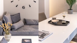 Uma sala de estar moderna com um sofá cinza, um relógio de parede e um vaso com flores secas.