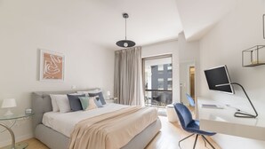 Quarto de hotel moderno com cama, escrivaninha, cadeira, televisão e janela com cortinas.