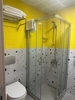 Casa de banho com chuveiro em cabine de vidro, sanita e porta-toalhas com toalhas.