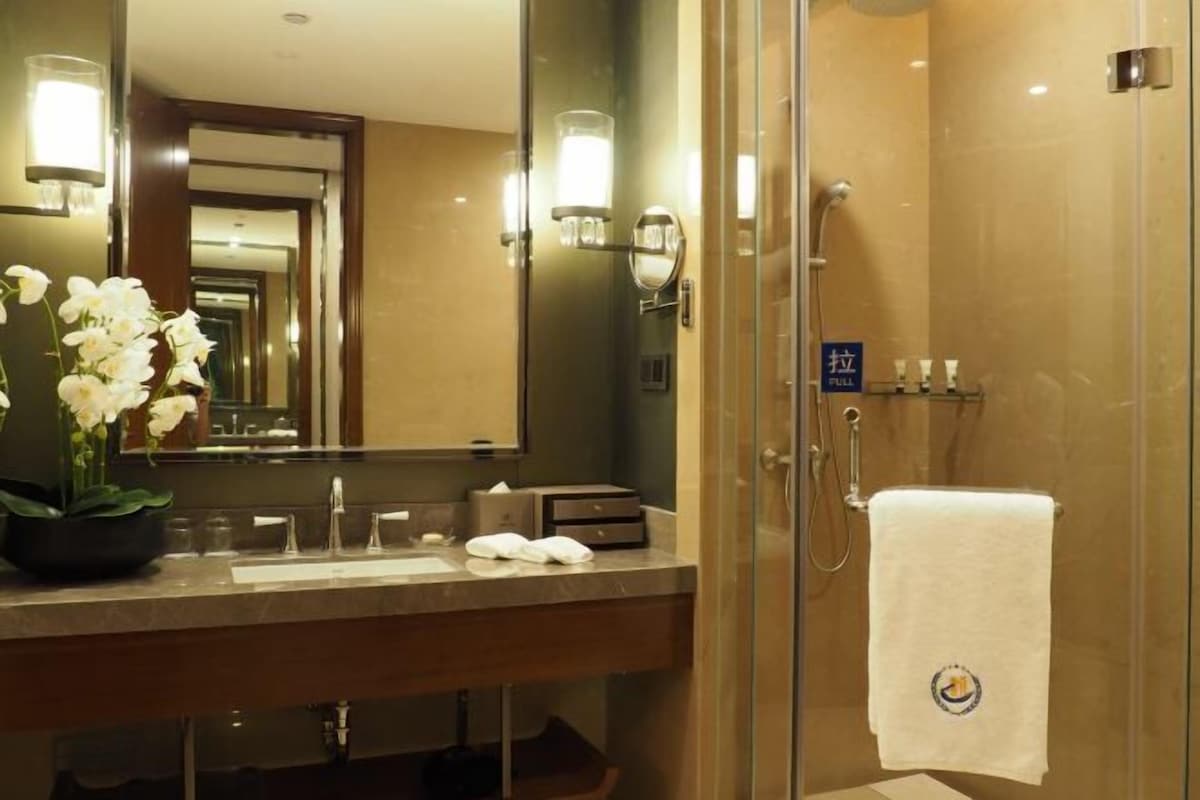 Casa de banho de hotel com cabine de chuveiro em vidro, uma pia com espelho e um porta-toalhas.