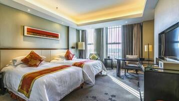 Quarto de hotel com duas camas, uma escrivaninha, uma cadeira, uma televisão e uma janela grande.