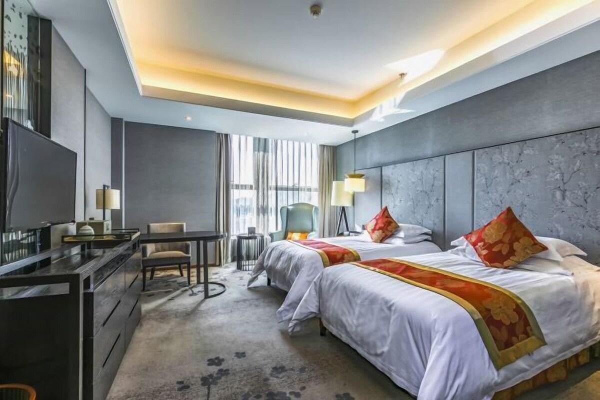 Quarto de hotel moderno com duas camas, uma mesa, uma cadeira e uma televisão.