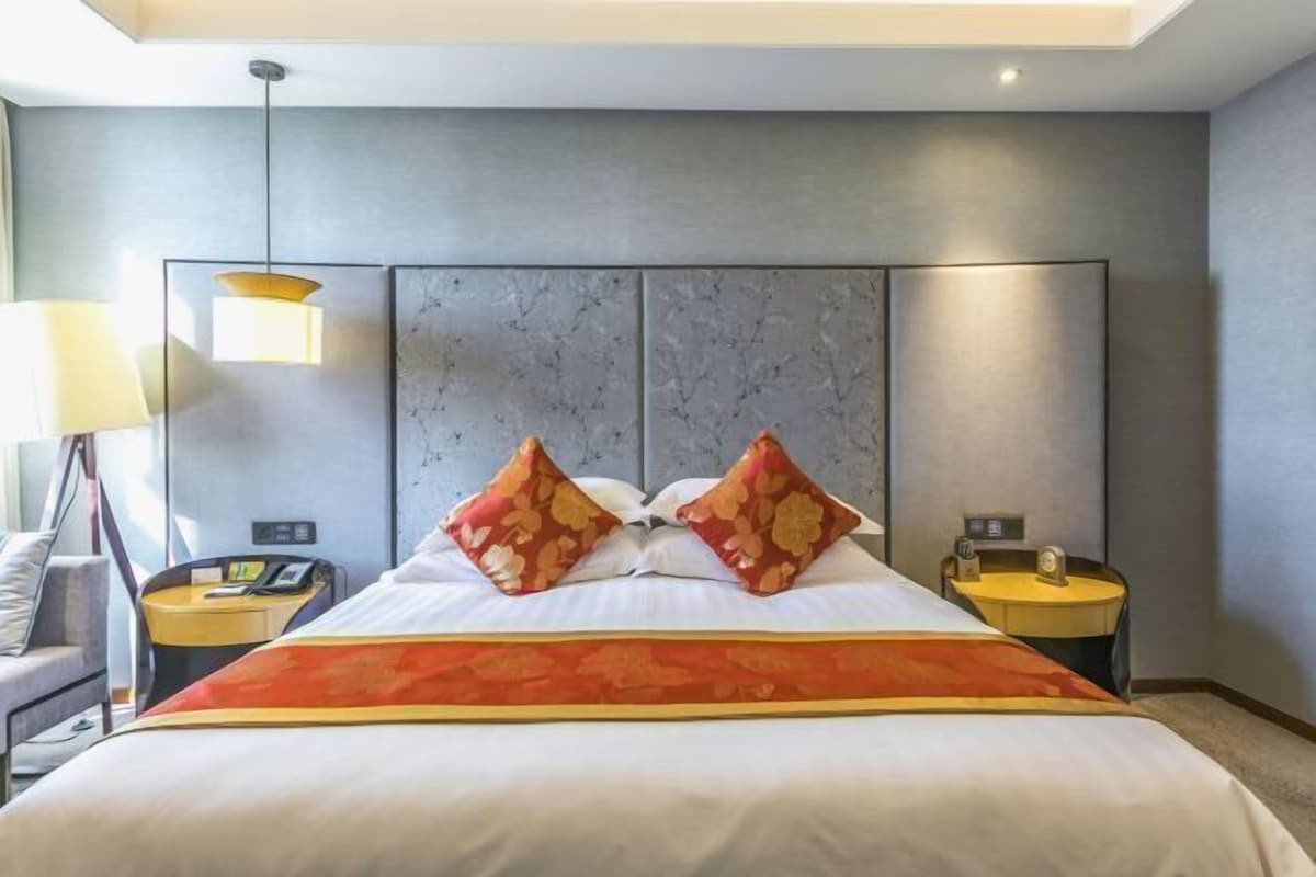 Quarto de hotel com uma cama grande, duas mesas de cabeceira, uma escrivaninha e uma cadeira.