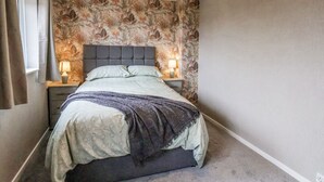 Quarto com cama, duas luminárias de cabeceira, papel de parede estampado e luminária no teto.