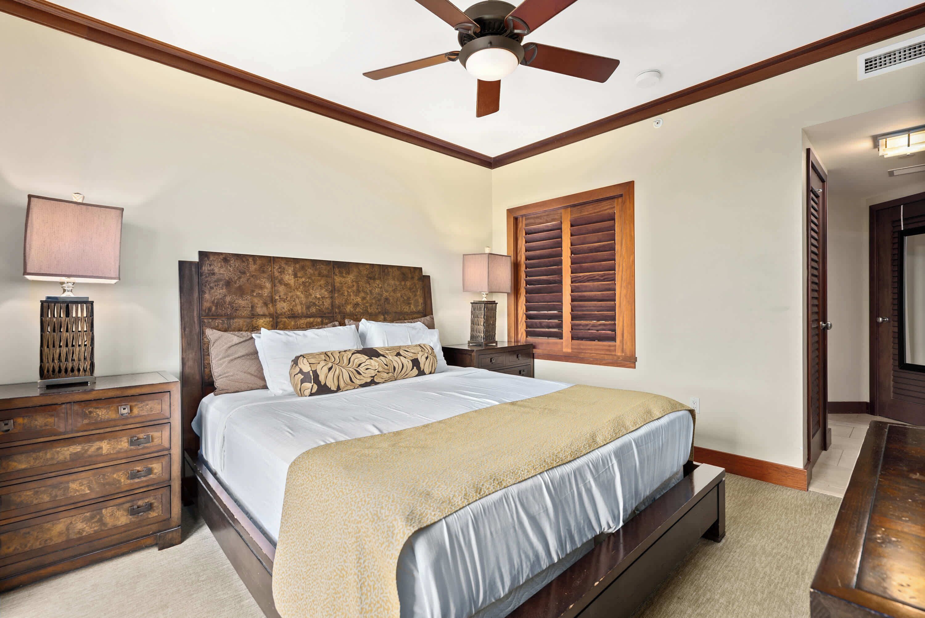 Quarto com cama grande, cabeceira de madeira e ventoinha no teto.