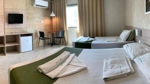 Quarto de hotel com duas camas, uma escrivaninha, uma cadeira, uma televisão e uma janela com cortinas.
