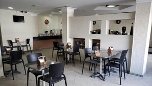 Uma área de jantar moderna com várias mesas e cadeiras, um balcão com estação de café e uma televisão na parede.
