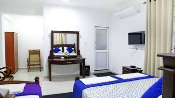 Quarto de hotel com cama, escrivaninha, cadeira, guarda-roupa, televisão e porta.