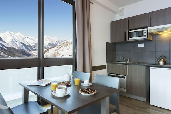 Cozinha moderna com vista para montanhas cobertas de neve, mesa de jantar com itens de café da manhã e micro-ondas compacto.