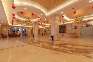 Um hall amplo com piso de mármore, balcão de recepção e um lustre.
