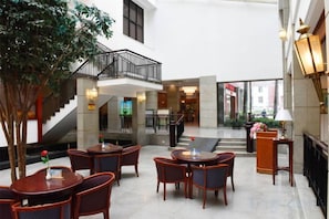 Um saguão de hotel com uma escadaria central, várias áreas de estar e uma grande planta de interior.