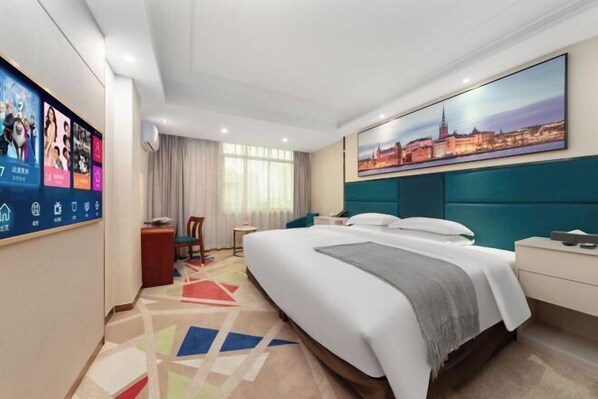 Quarto de hotel com uma cama grande, escrivaninha, cadeira e televisão exibindo cartazes de filmes.