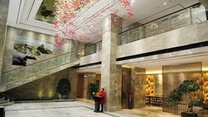 Um hall amplo com piso de mármore, uma escadaria imponente e uma área de recepção com um funcionário.