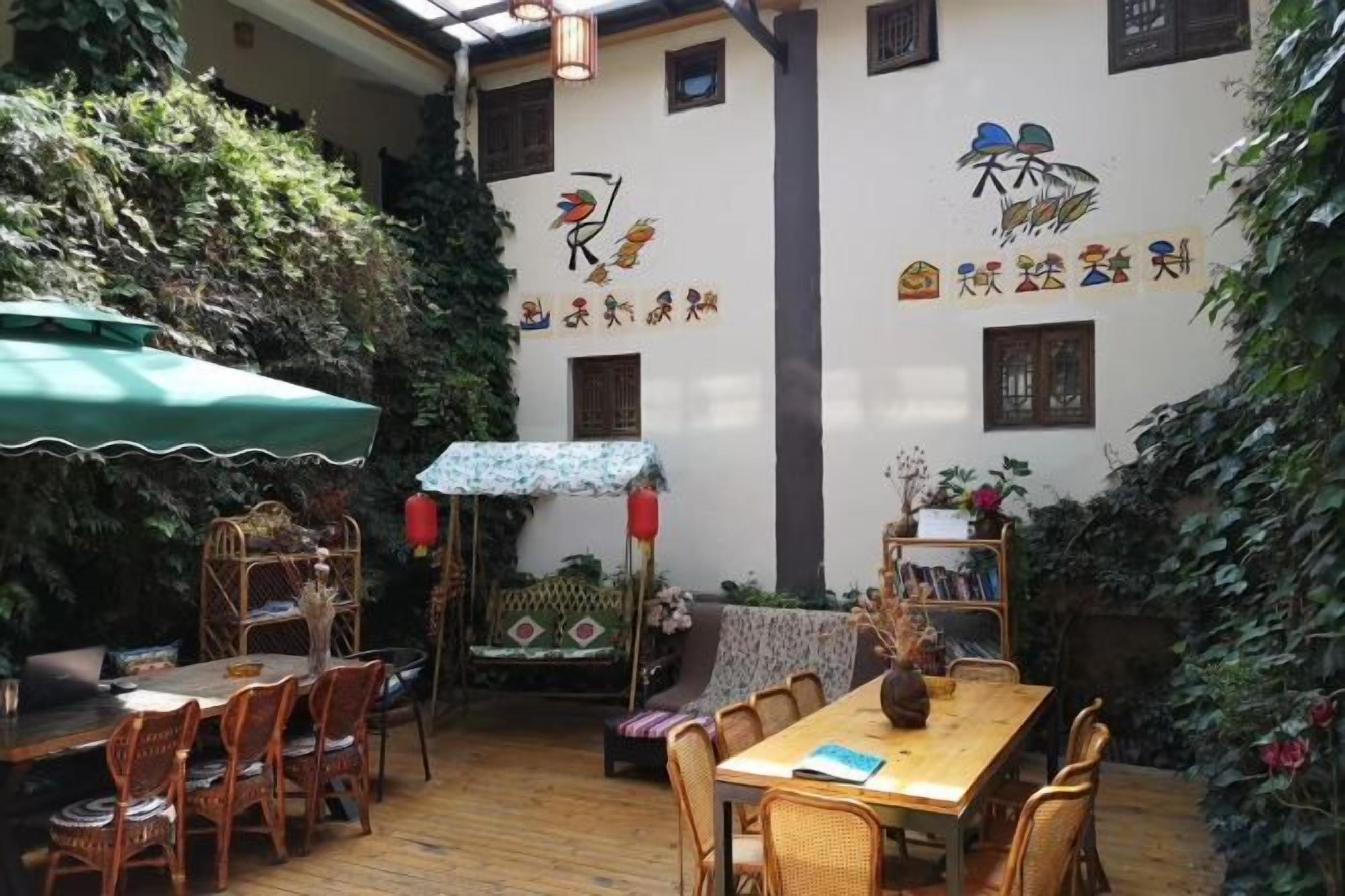 Um pátio externo com móveis de madeira, uma mesa e um guarda-sol verde.