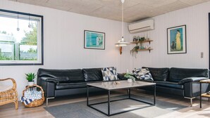 Uma sala de estar moderna com um sofá de couro preto, uma mesa de centro de madeira e uma janela grande com vista para o verde.