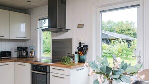 Uma cozinha moderna com armários brancos, uma coifa de aço inoxidável e vista para uma casa através de uma janela grande.