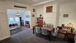 Uma sala de estar com sofá, mesa de centro e TV, uma área de jantar com mesa e cadeiras, e uma cozinha com fogão e armários.