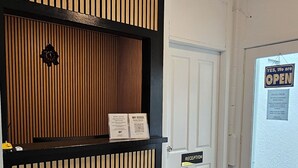 Uma área de recepção com parede de ripas de madeira, balcão de atendimento e uma porta com a inscrição 'RECEPTION'.