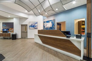 Uma área de recepção moderna, com um balcão de madeira, um ecrã digital e uma estação de café.
