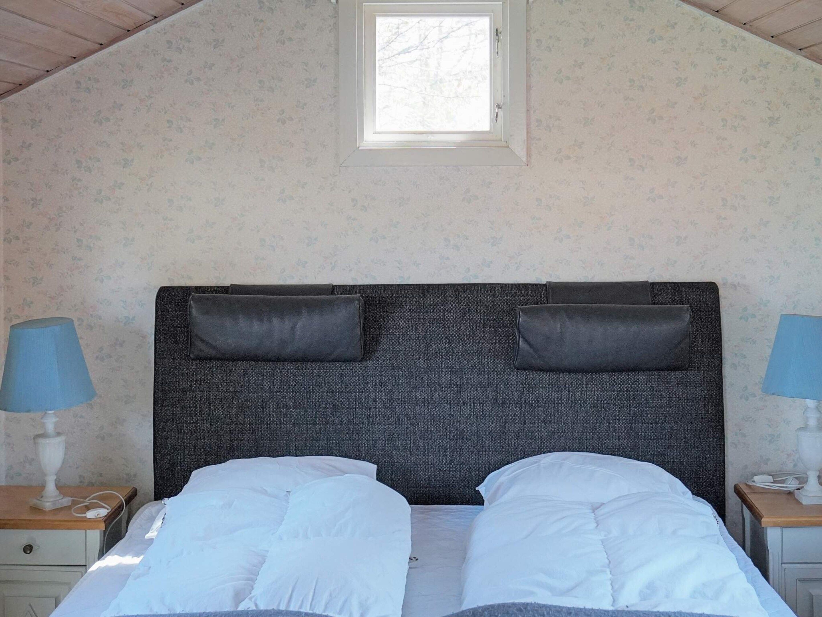 Quarto com cama, duas mesas de cabeceira, janela e parede com papel de parede floral.