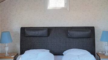 Quarto com cama, duas mesas de cabeceira, janela e parede com papel de parede floral.