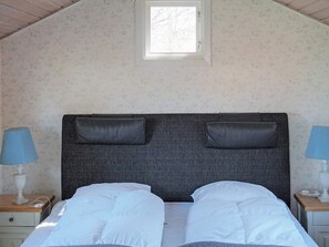 Quarto com cama, duas mesas de cabeceira, janela e parede com papel de parede floral.