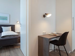 Quarto de hotel moderno com cama, mesa de cabeceira, luminária e escrivaninha com cadeira.
