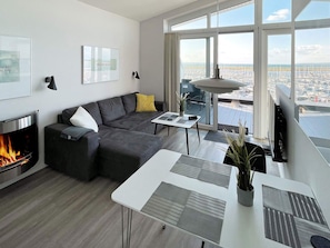 Sala de estar moderna com lareira, sofá, mesa de jantar e vista para a marina através de amplas janelas.