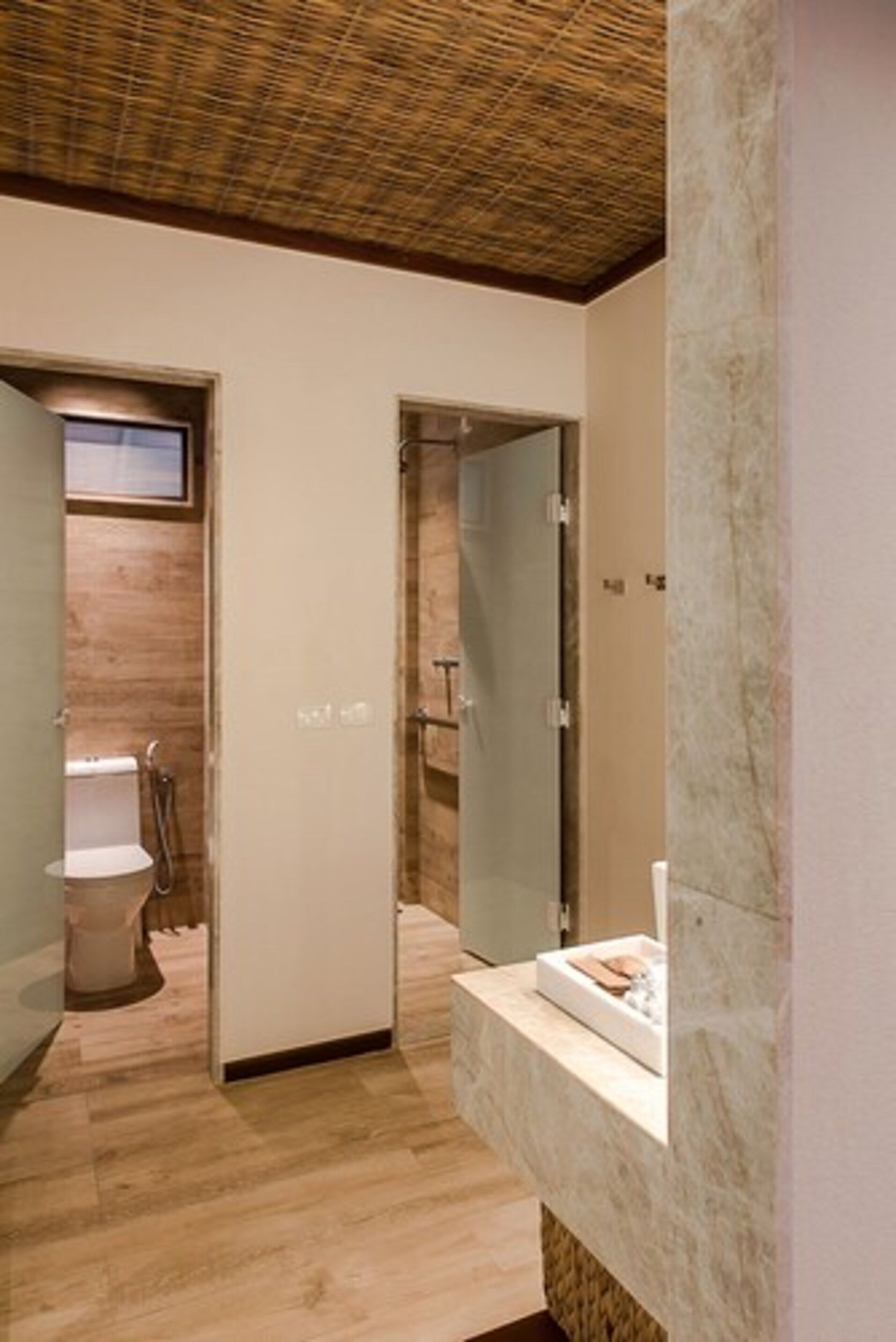 Um banheiro moderno com piso de madeira, box de vidro e bancada de mármore.