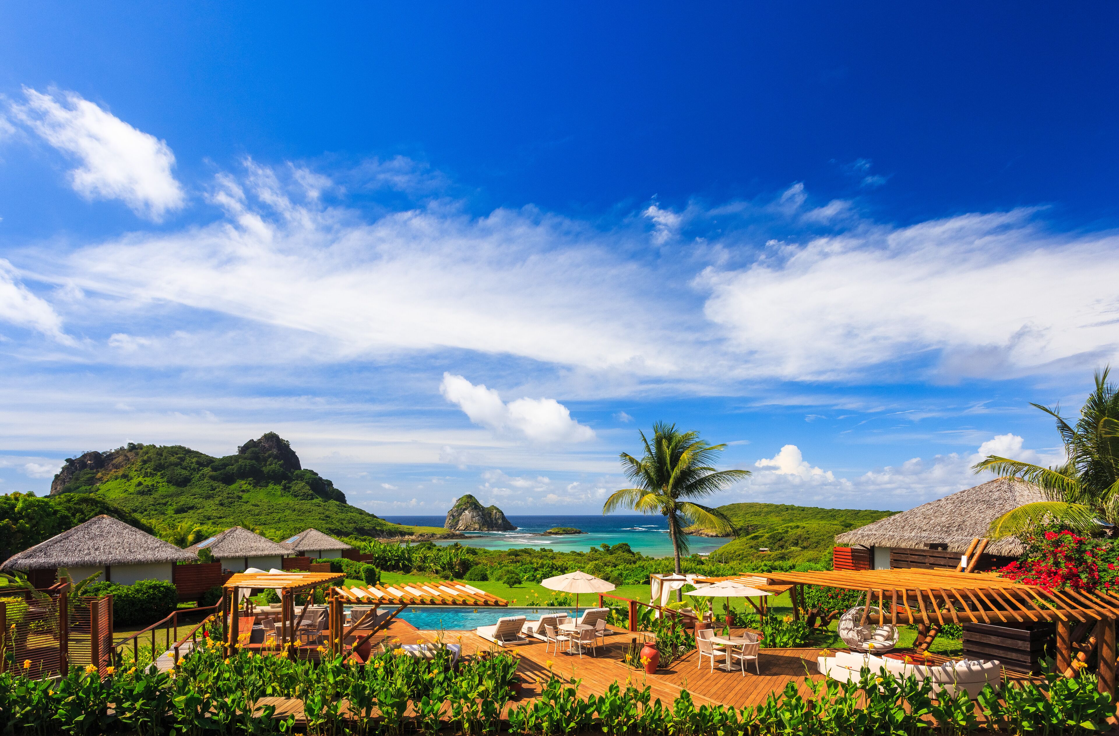 Um resort com cabanas de telhado de palha, piscina e vista para o oceano.