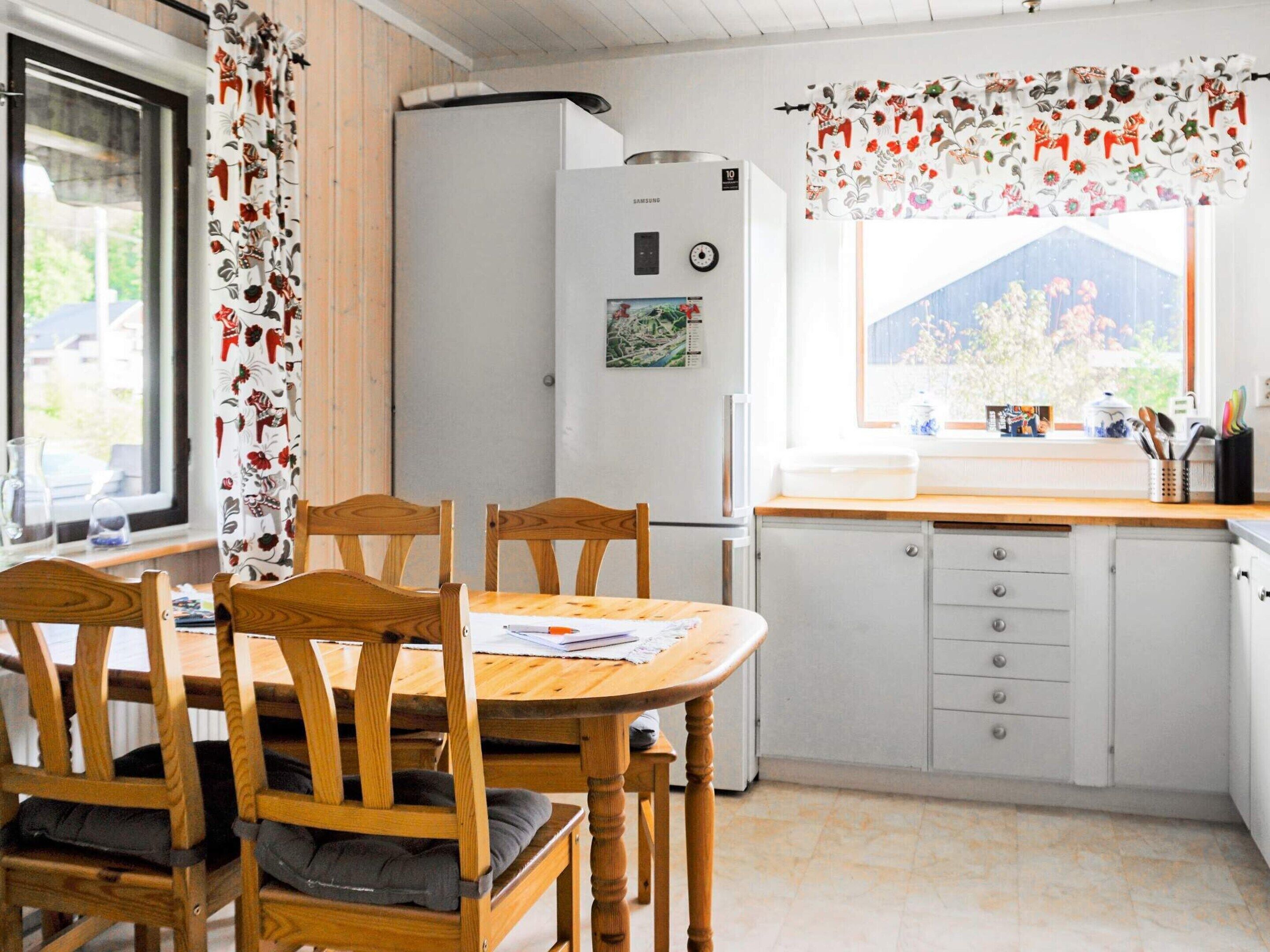Cozinha com geladeira, cadeiras de madeira, mesa de jantar e janela com cortinas.