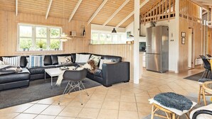 Uma sala ampla com um grande sofá preto, uma mesa de centro e um espaço de jantar com uma mesa redonda e cadeiras.