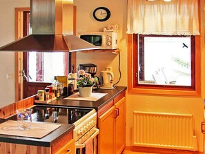 Cozinha compacta com fogão, forno, micro-ondas e um relógio na parede.