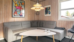 Uma sala de estar moderna com um sofá seccional cinza, uma mesa de centro branca arredondada e uma janela grande.