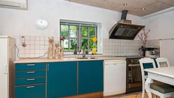 Cozinha com armários verde-água, lava-louças branco e janela com vista para área verde.