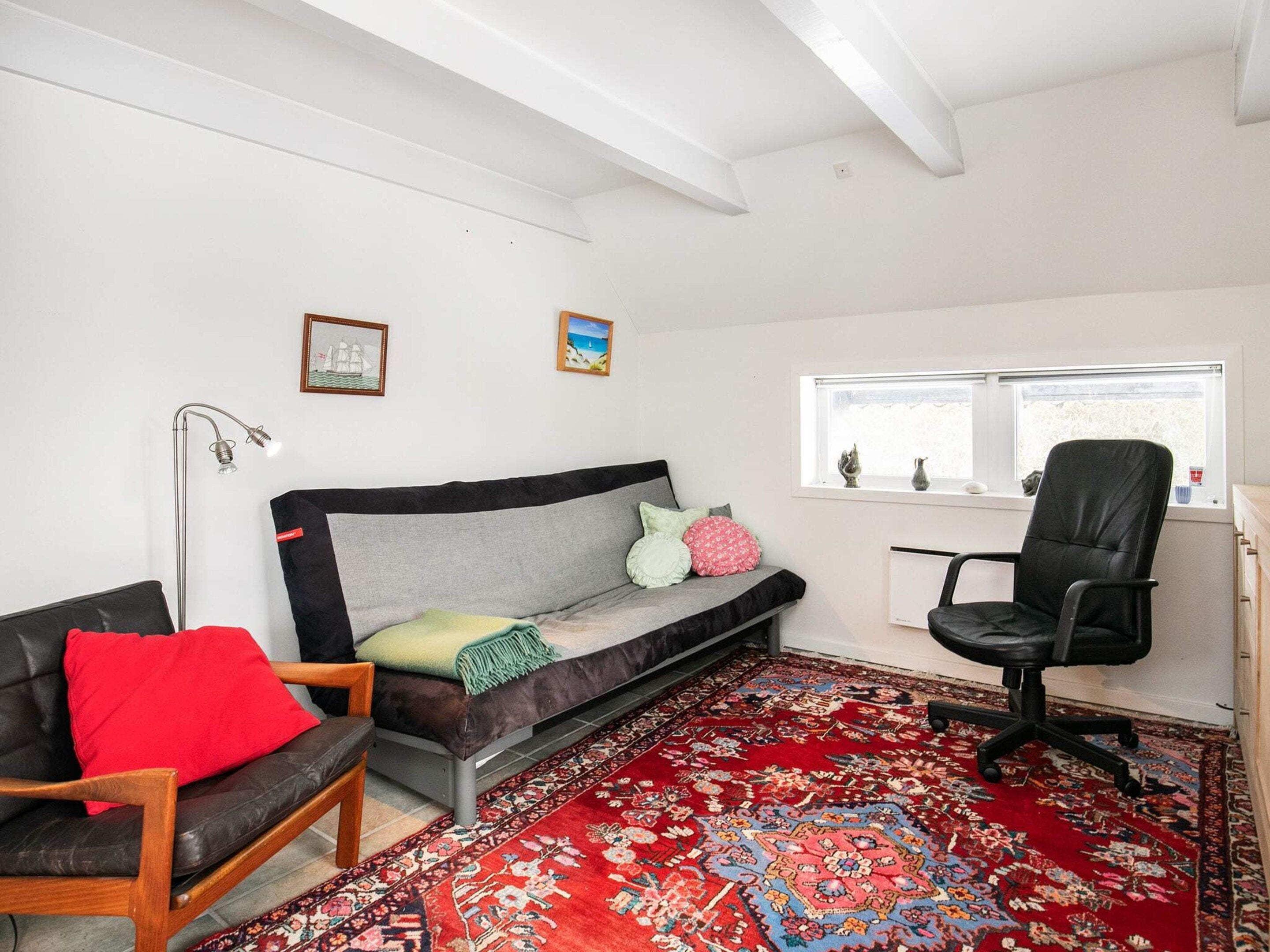 Quarto com sofá, poltrona, escrivaninha, janela e tapete estampado.