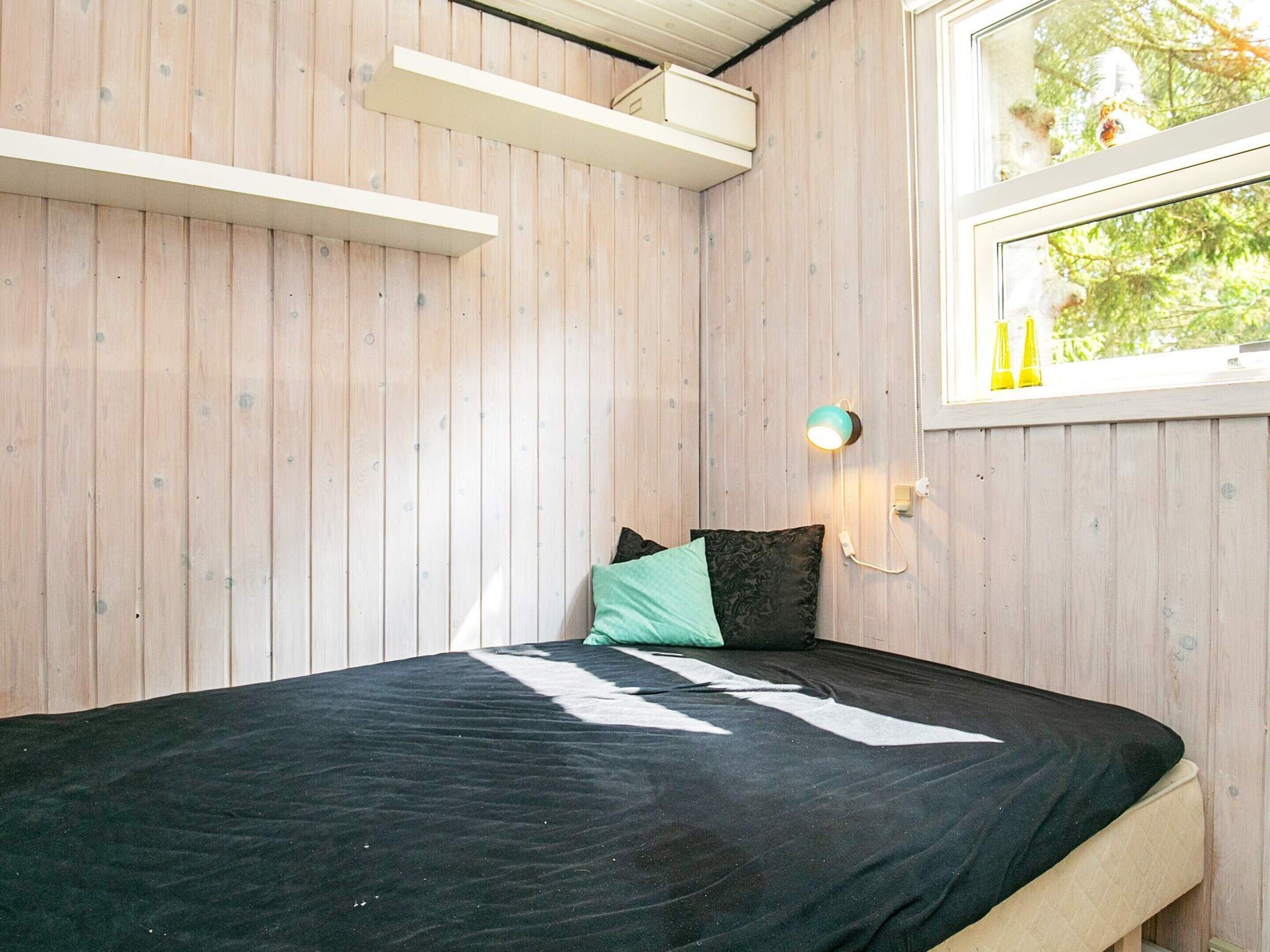 Quarto com cama, janela com vista para árvores e luminária fixada na parede.