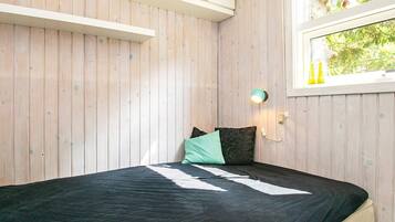 Quarto com cama, janela com vista para árvores e luminária fixada na parede.