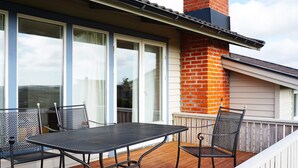 Um terraço com mesa e cadeiras, chaminé de tijolos e grandes portas de vidro deslizantes.