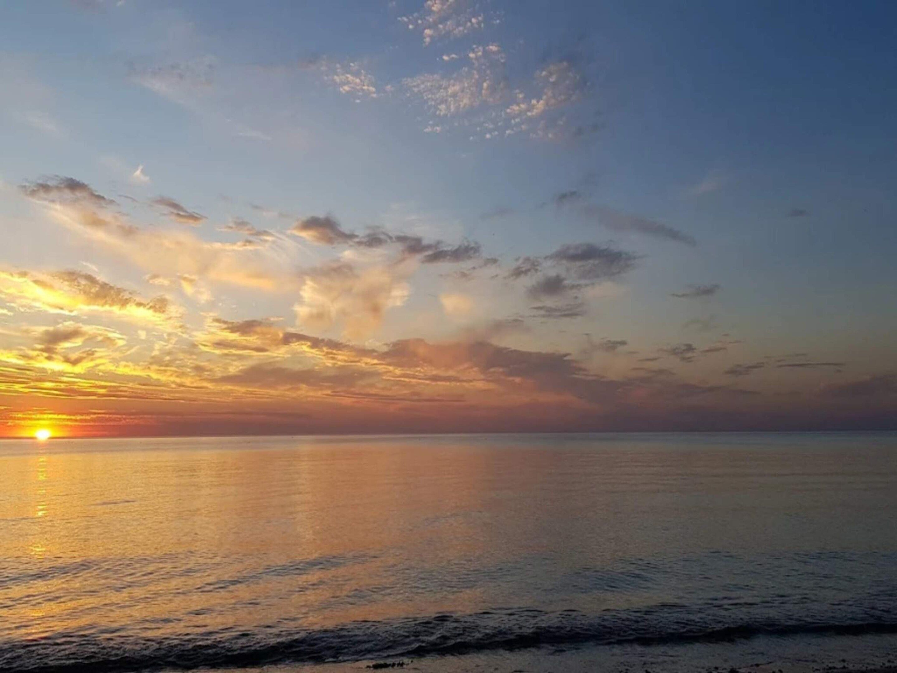 Um pôr do sol sobre um mar calmo, com o horizonte nítido.